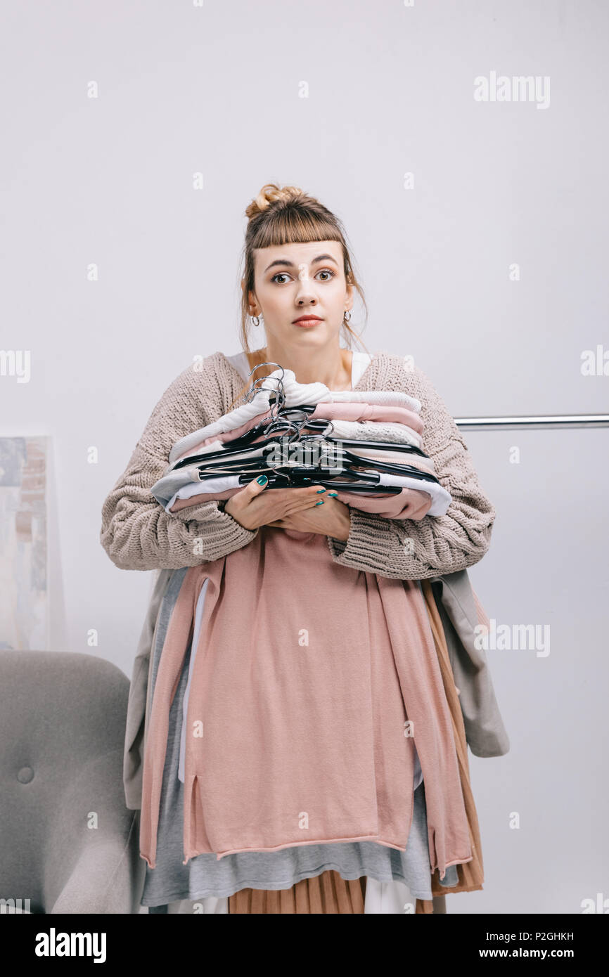 surprised girl holding stack of clothes on hangers and looking at ...