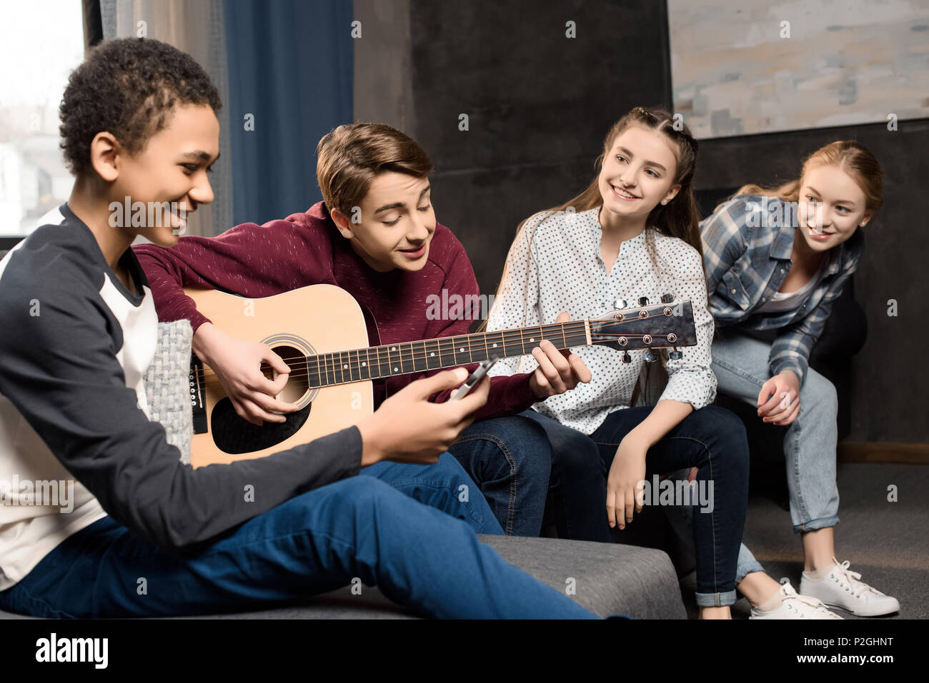 boy playing acustic guitar and singing while his friends listening at ...