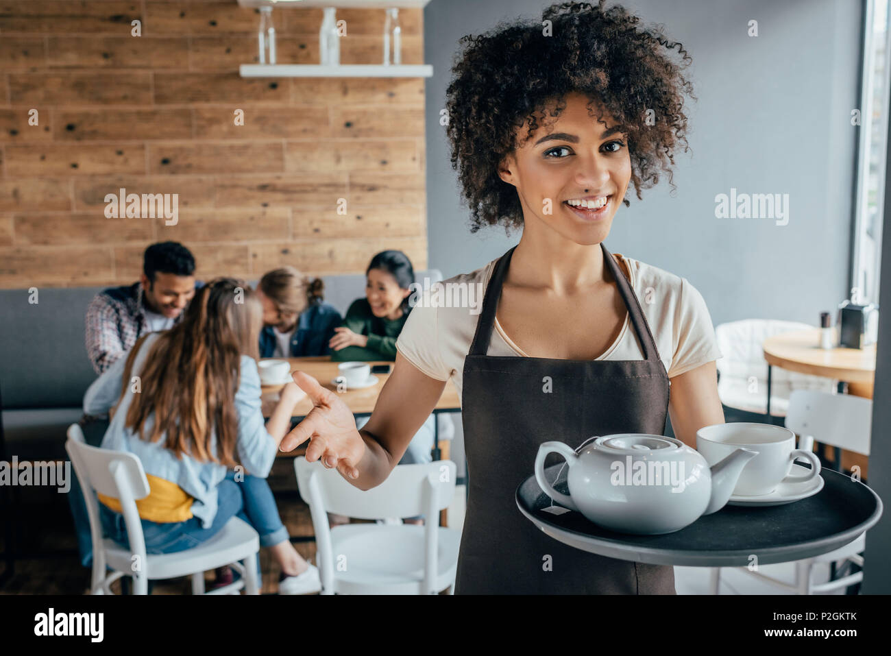 Smiling african american waitress holding tray with tea and customers ...
