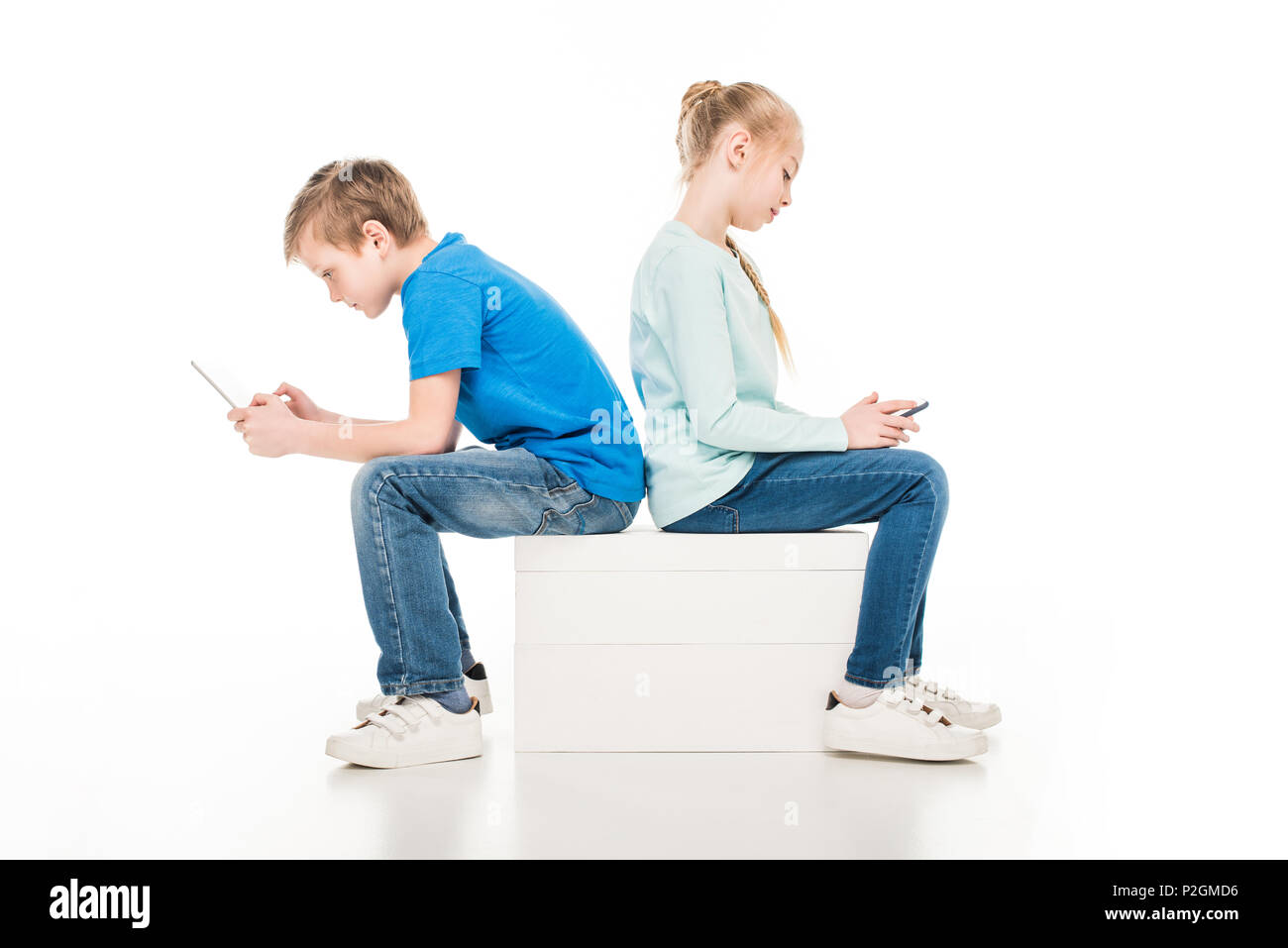 side view of kids using digital devices while sitting back to back ...