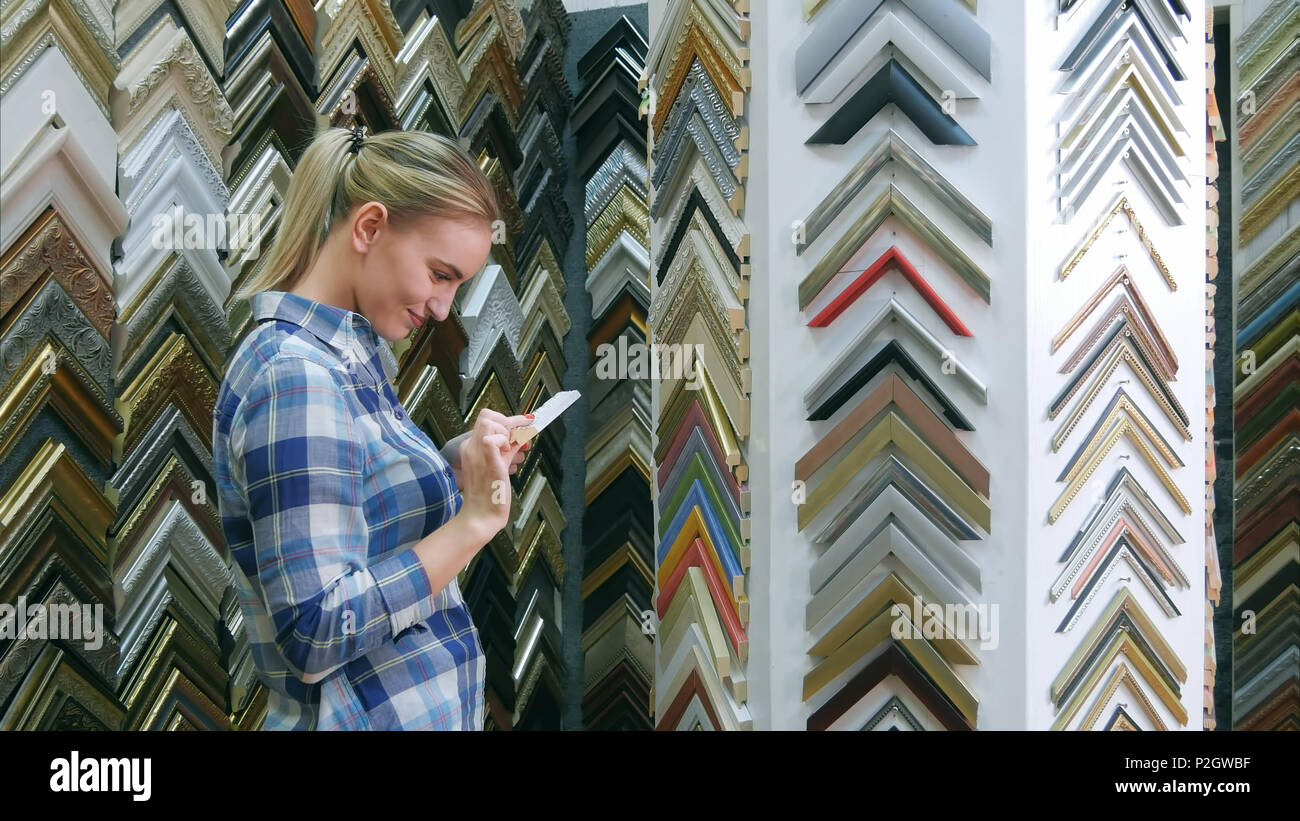 Smiling female customer looking for frame, standing near frame stand in ...