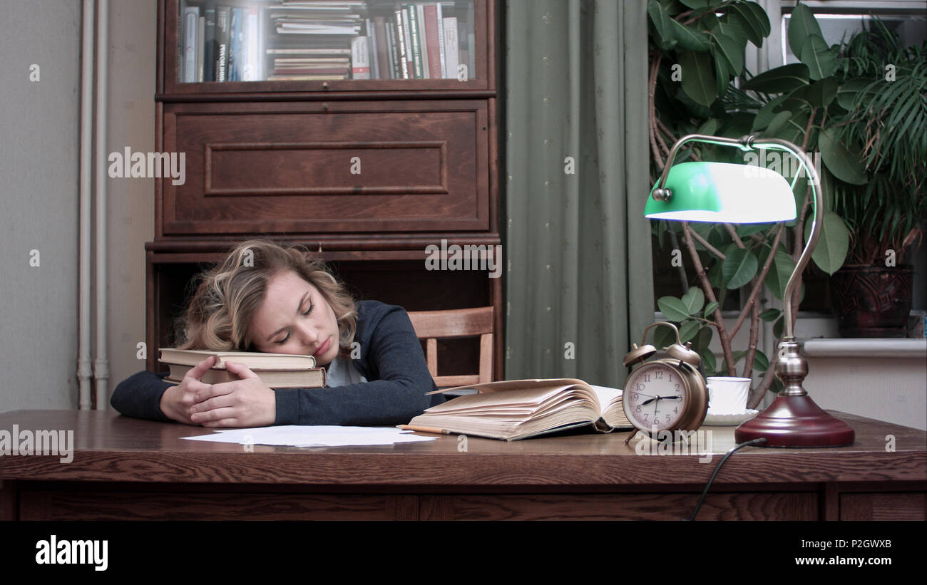 Tired female taking a nap on pile of books at her workplace and being ...