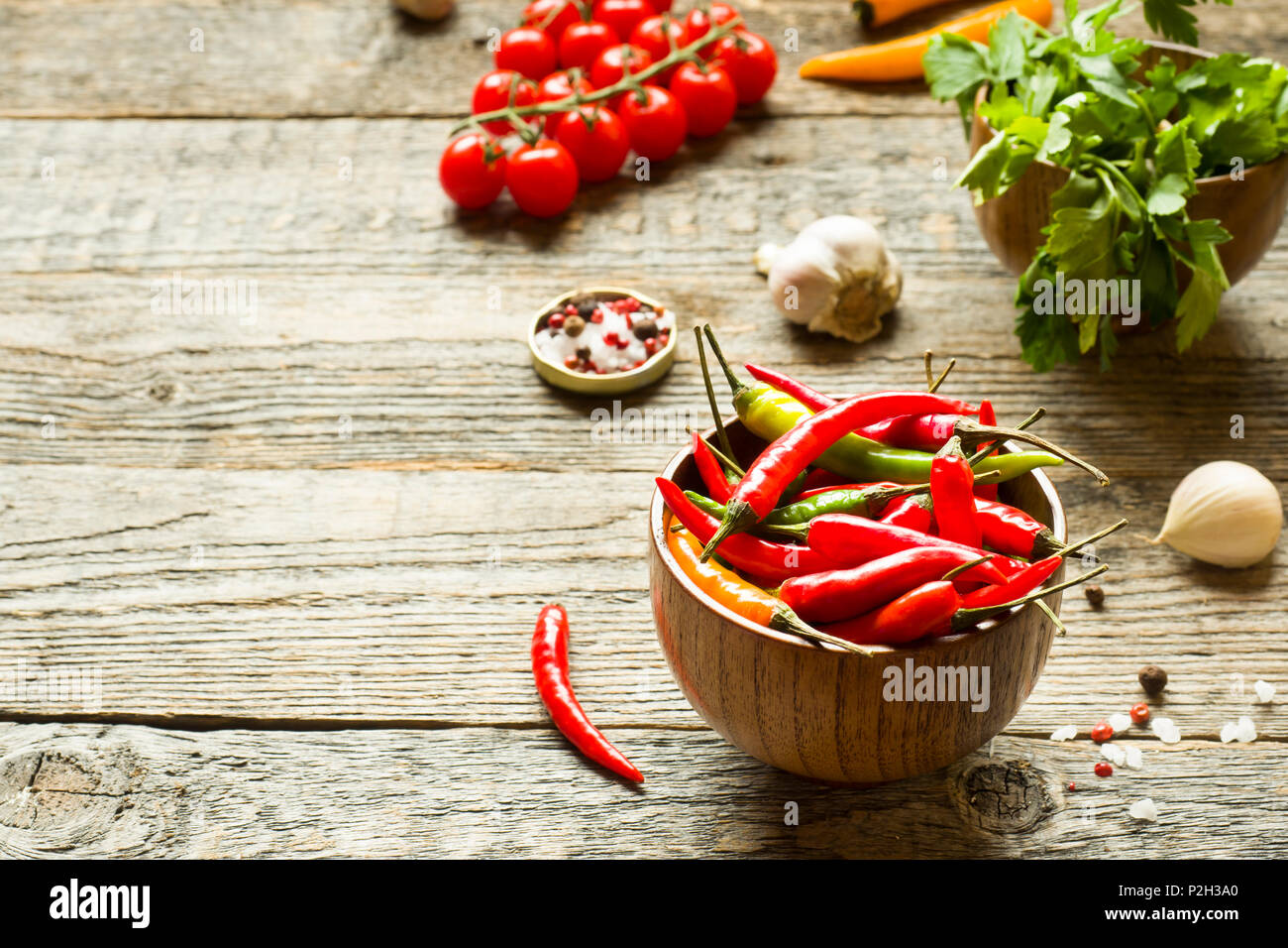 Chili pepper is spicy in a wooden bowl. Tomato parsley garlic on wooden ...