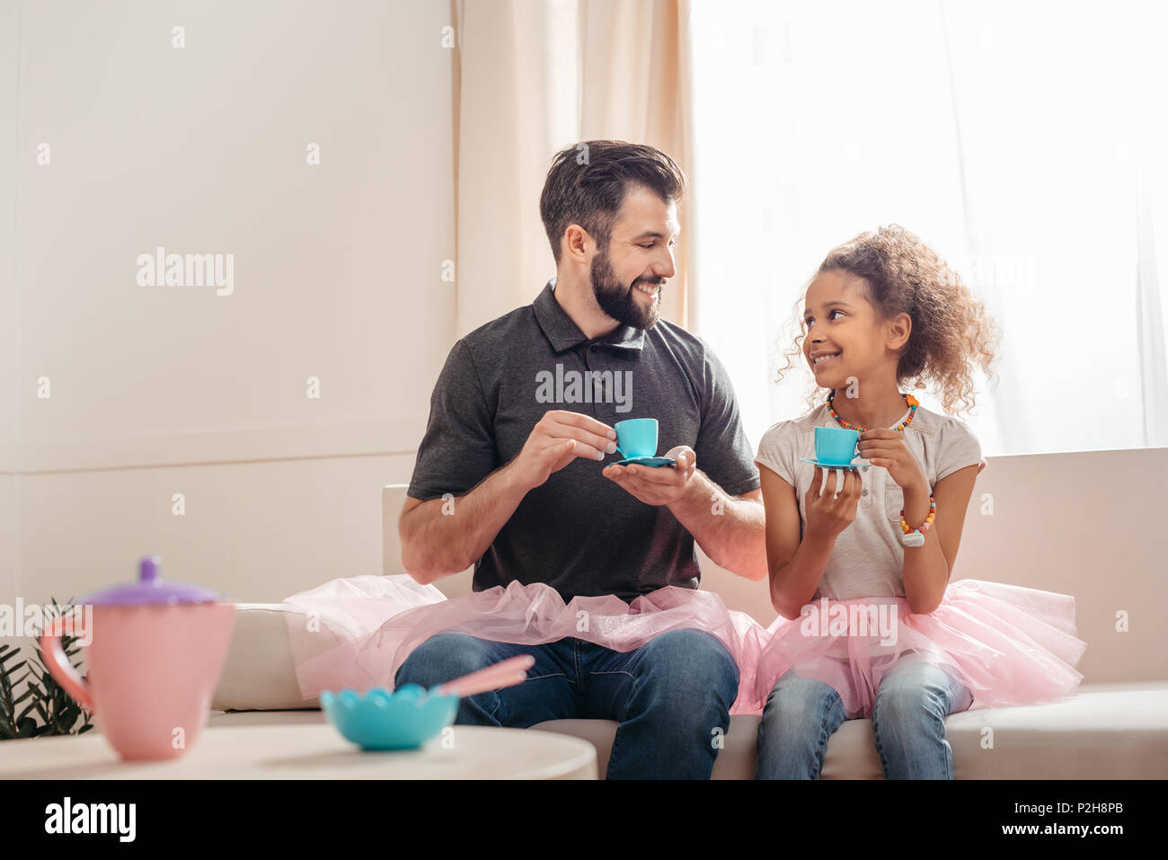 multicultural father and smiling daughter having tea party at home ...