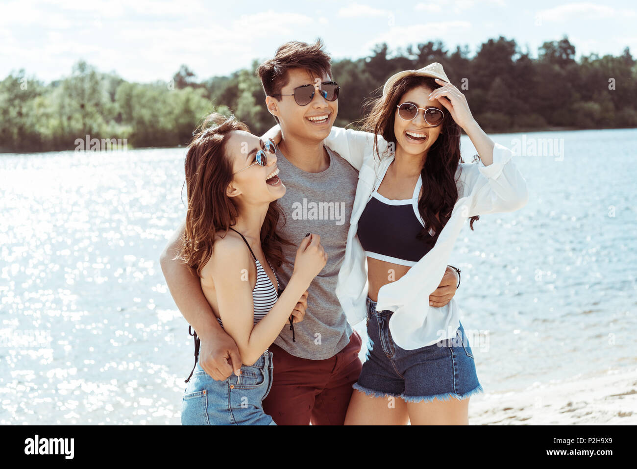 cheerful friends hugging each other and looking away on beach Stock ...