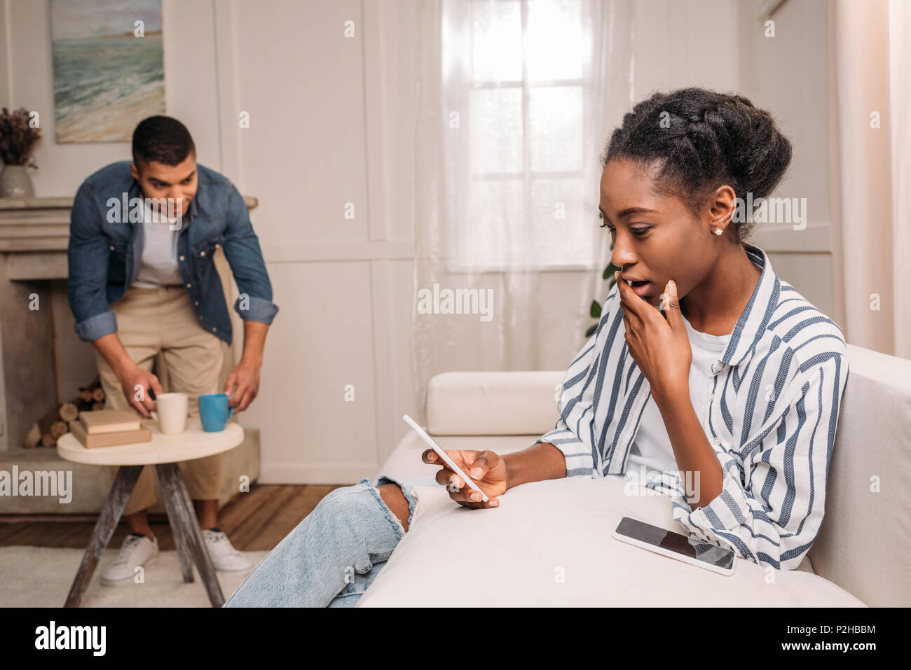 young african american woman on couch using smartphone and man putting ...