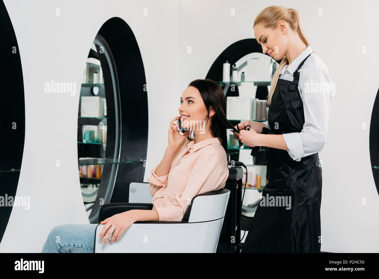 woman talking by smartphone while hairdresser cutting hair Stock Photo ...