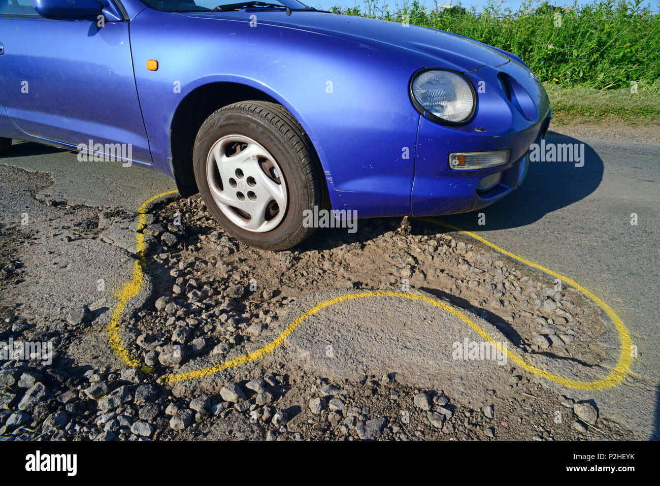 car driving over enormous pot hole on road marked with yellow outline ...