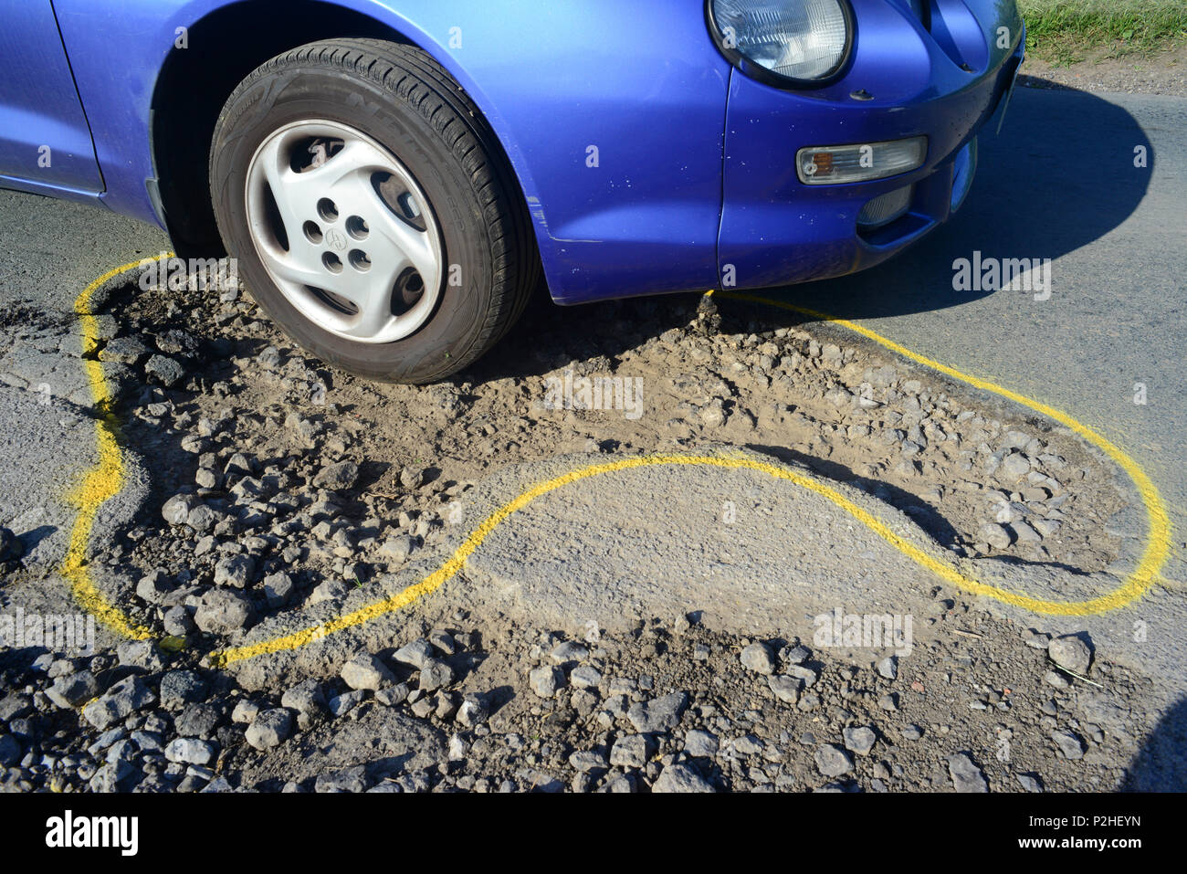 car driving over enormous pot hole on road marked with yellow outline ...