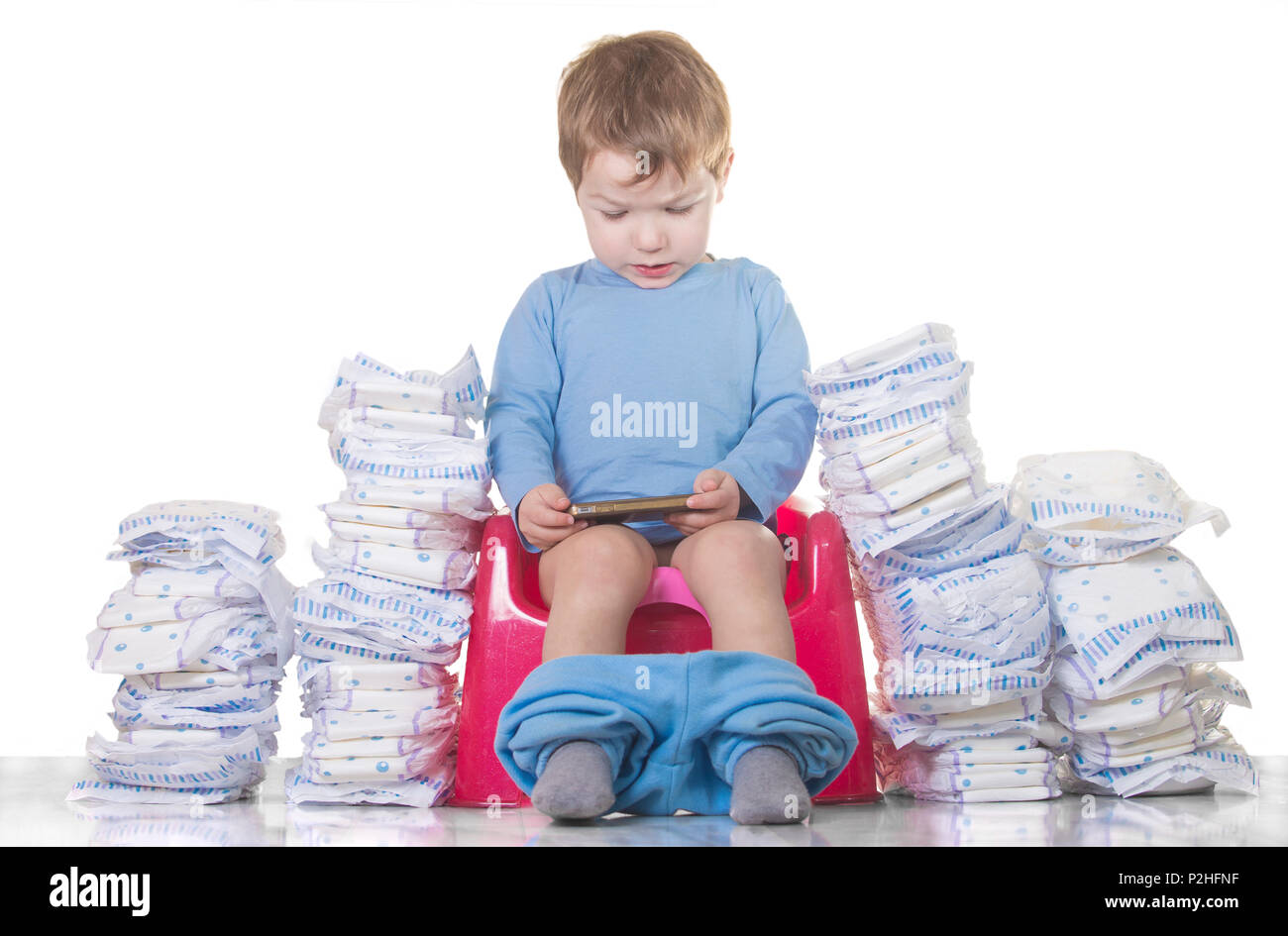 Baby boy sitting on chamber pot with smartphone and toilet paper rolls ...