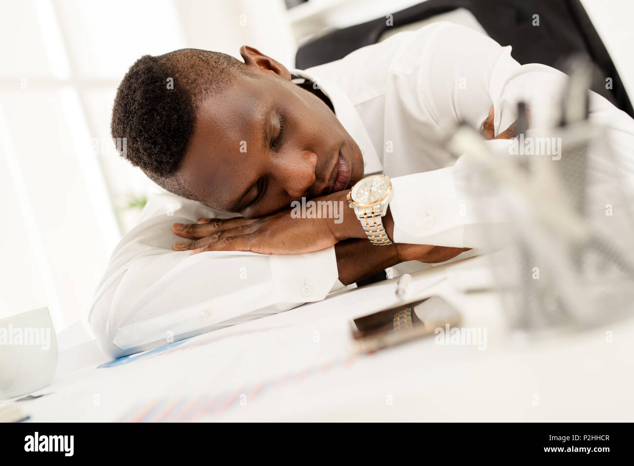 African businessman napping on desk next to documents late in the ...