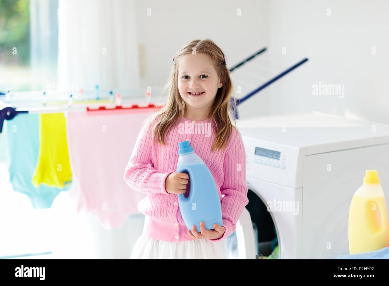 Child in laundry room with washing machine or tumble dryer. Kid helping ...