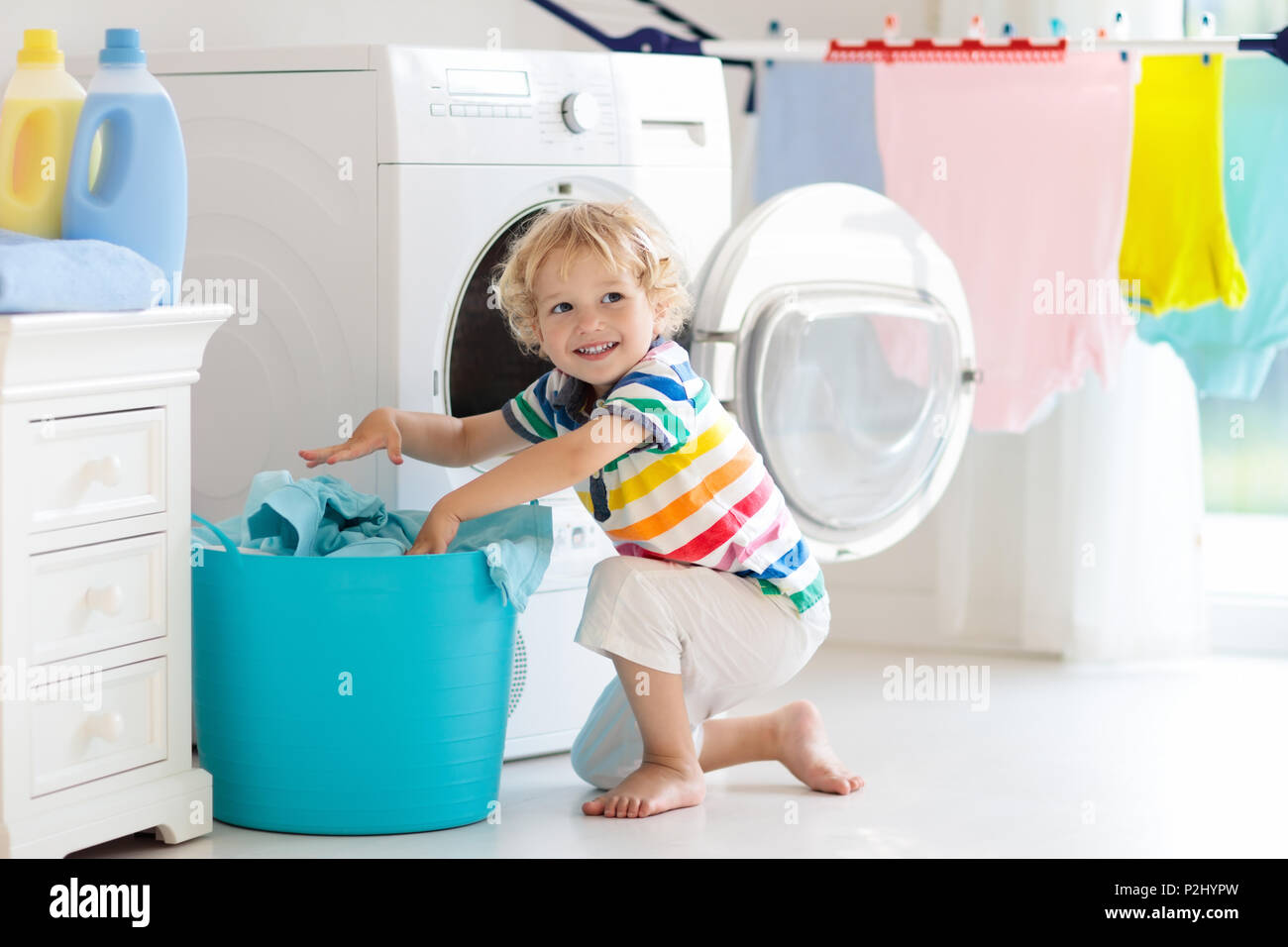 Child in laundry room with washing machine or tumble dryer. Kid helping ...