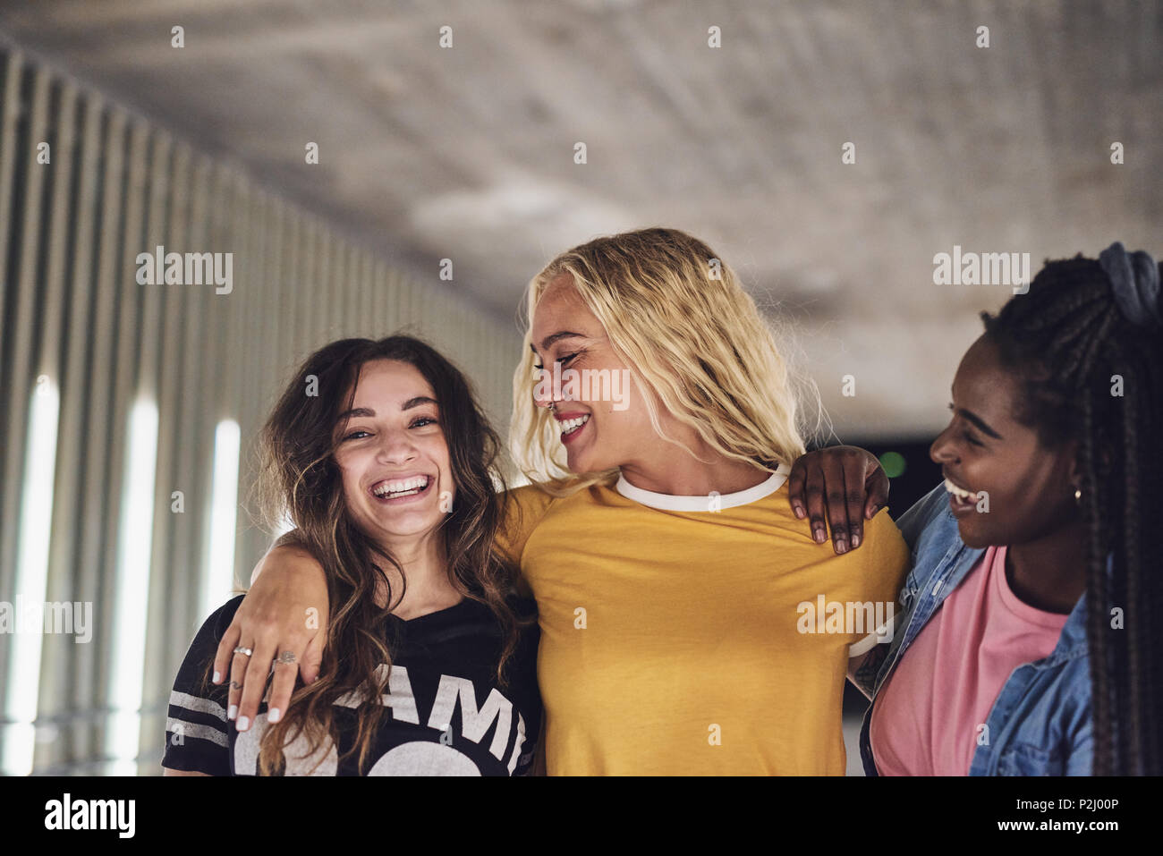 Three young girlfriends walking together down a walkway in the city at ...