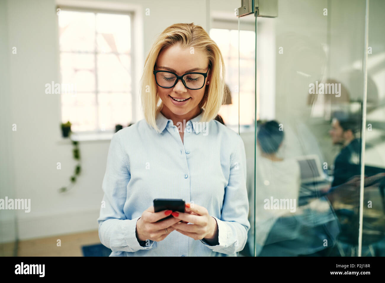 Smiling young businesswoman sending text messages on her cellphone ...