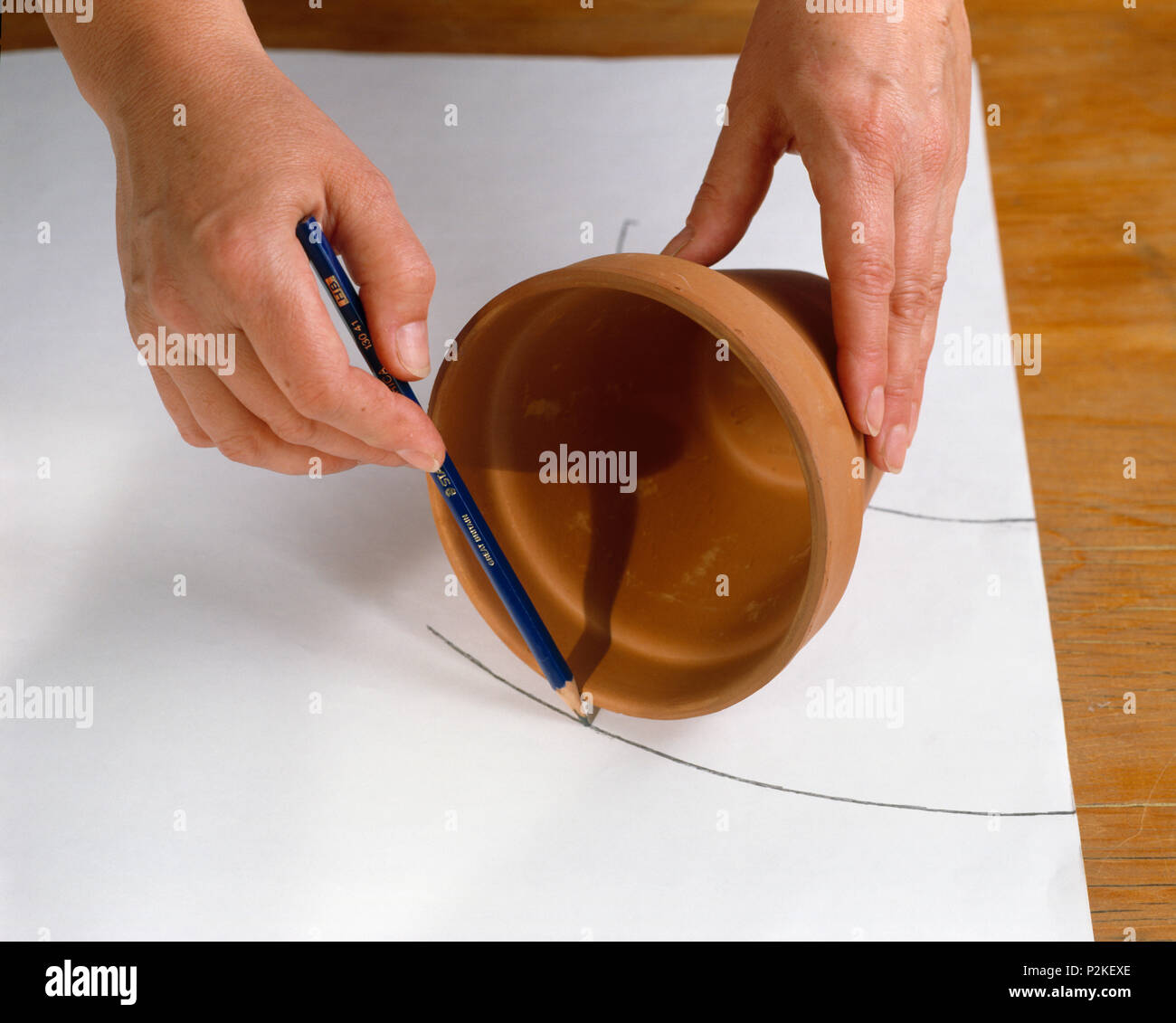 Close-up of hand drawing round terracotta flower pot on to white paper ...