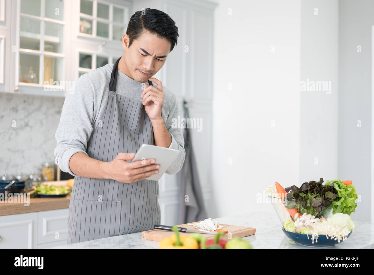 Asian confused man reading his tablet with a pensive thoughtful look ...