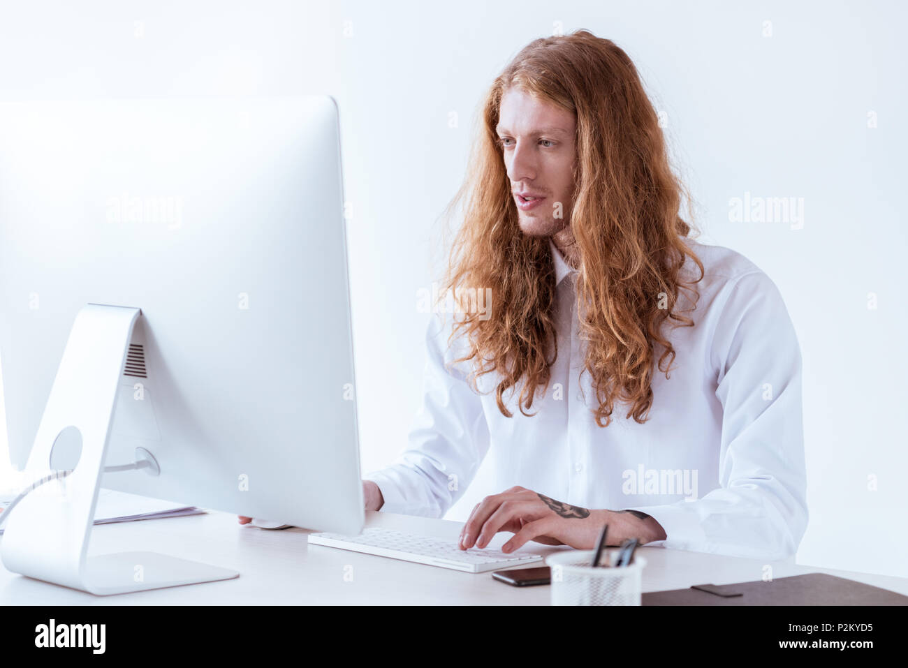 stylish tattooed businessman with ginger long hair working with ...