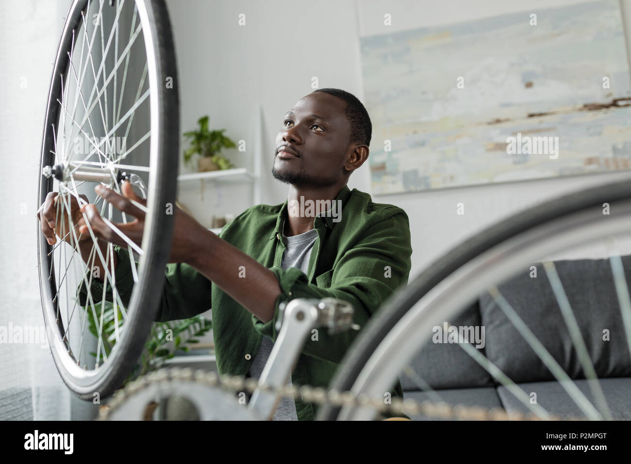 close-up view of handsome afro man checking bicycle wheel at home Stock ...