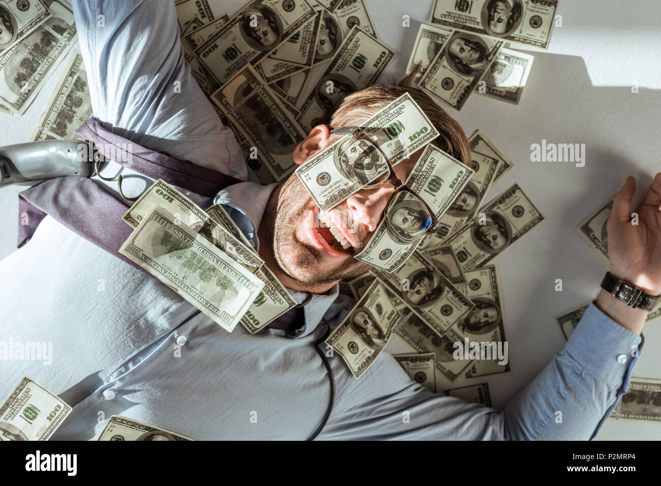 Young happy rich businessman lying on floor with dollar bills covering ...
