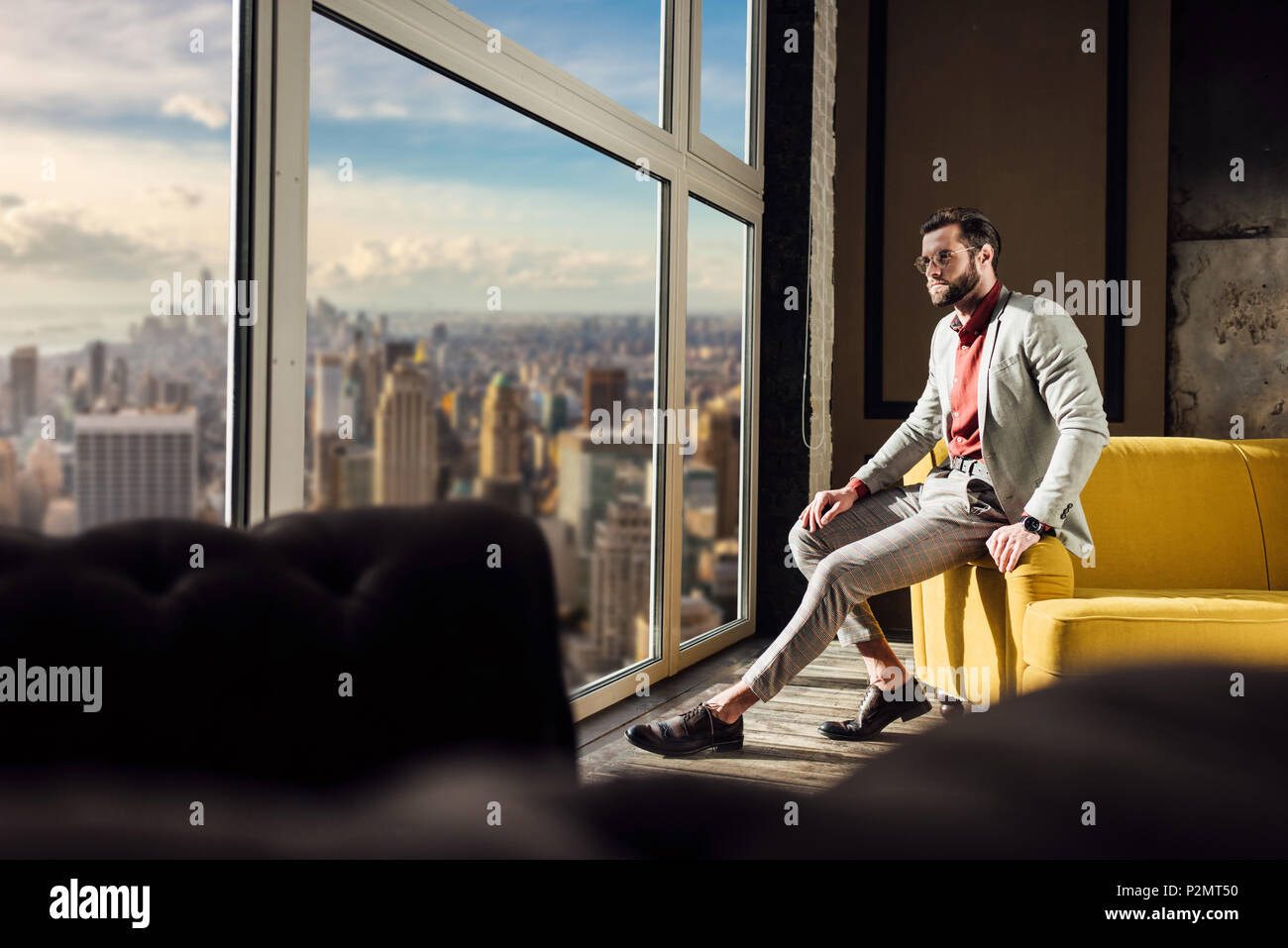 fashionable elegant man in stylish suit posing at window with city view ...