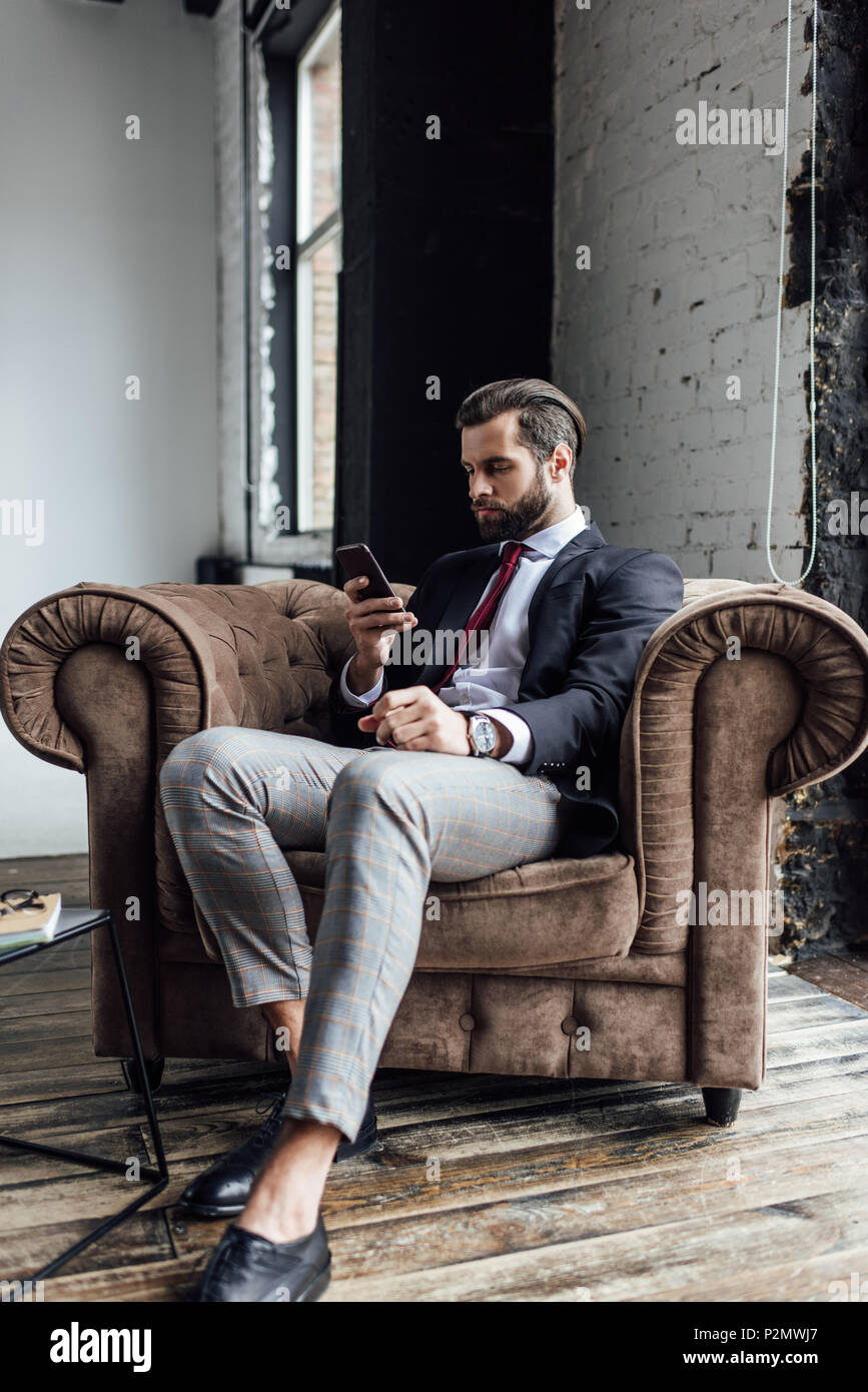 confident businessman texting sms on smartphone while sitting in ...