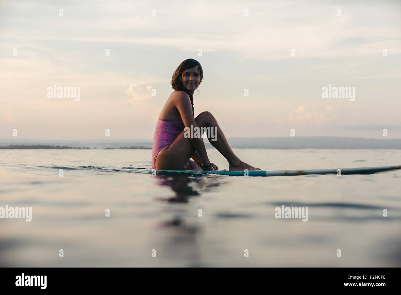 beautiful girl sitting on surfboard in water in ocean at sunset Stock ...