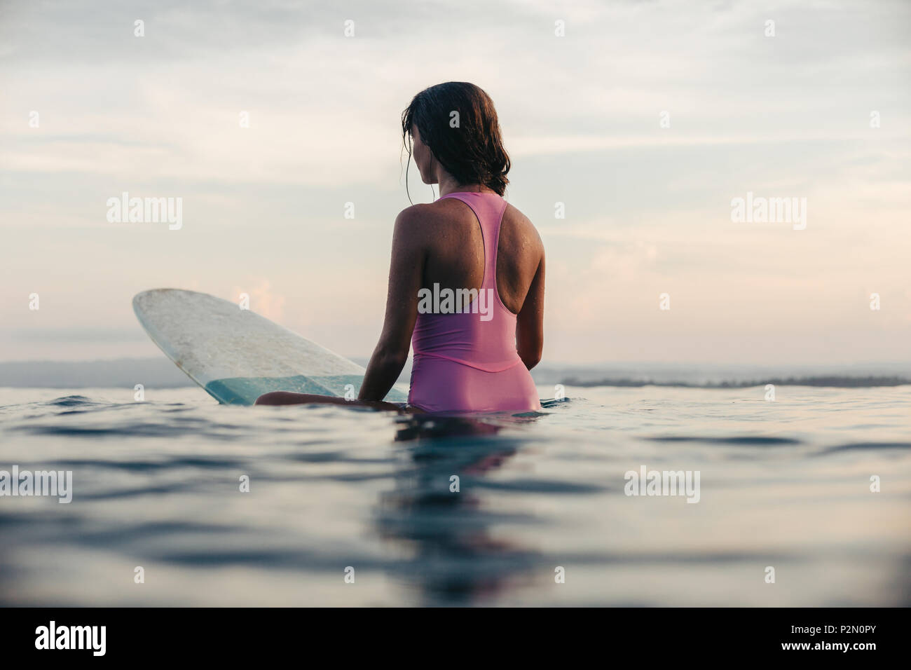 back view of girl sitting on surfboard in ocean at sunset Stock Photo ...