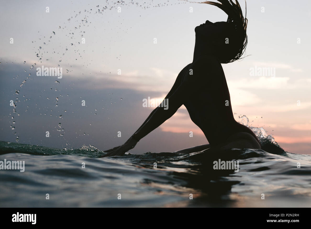 silhouette of woman whipping hair while resting on surfing board in ...