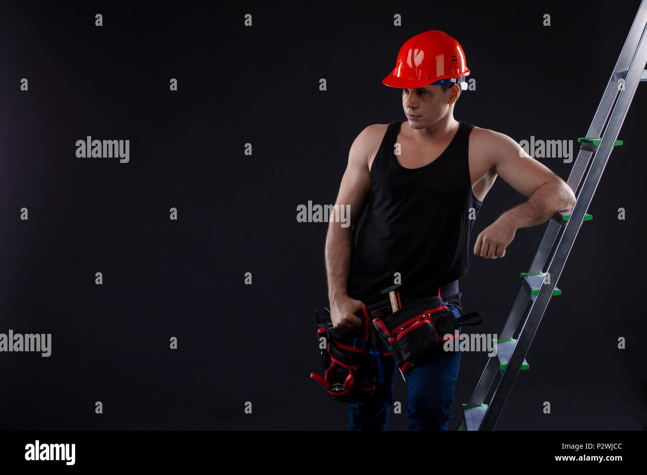Worker leans on a ladder and looks up on a black background. helmeted ...