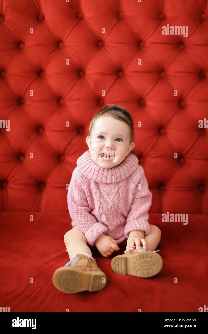 Little female baby sitting in red background on sofa Stock Photo - Alamy