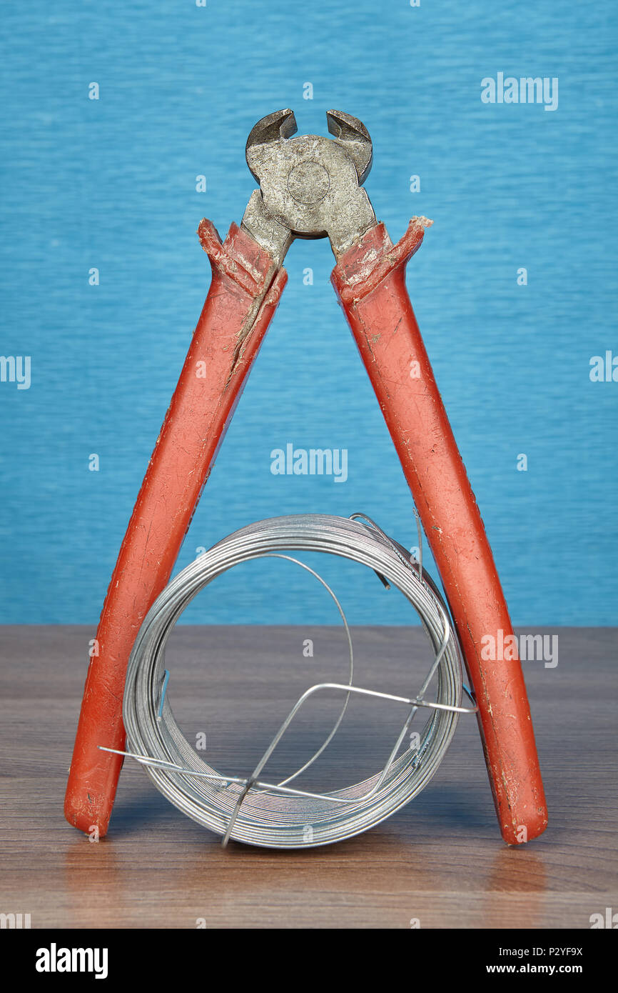 End cutter pliers with red plastic handles and steel wire coil lies on ...
