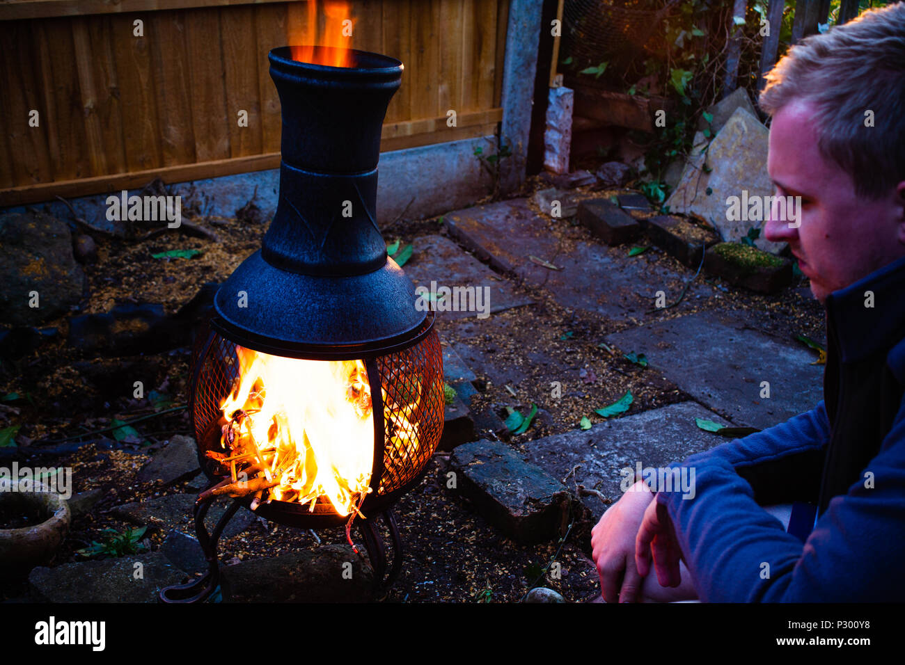 Young man sitting by the open fire in the twilight. Moody photo of man ...