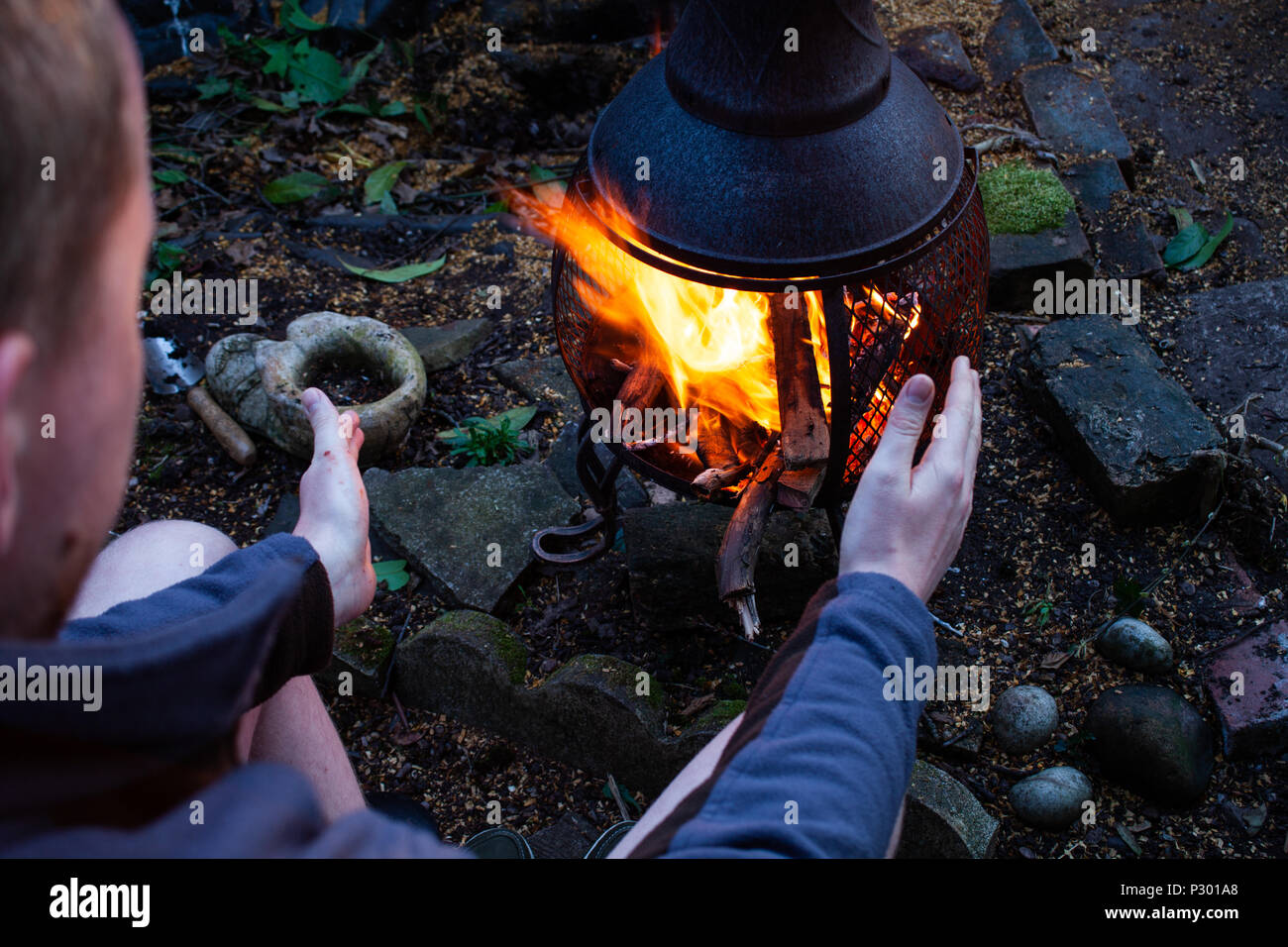 The man heats his hands in front of an open fire. Camping concept with ...