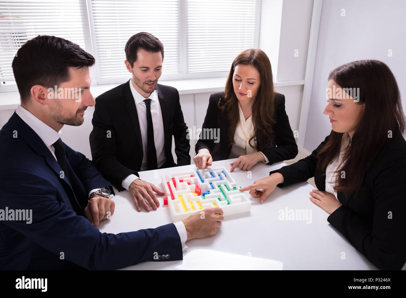 Young Businesspeople Holding Multi Colored Arrow Solving Maze On Desk ...