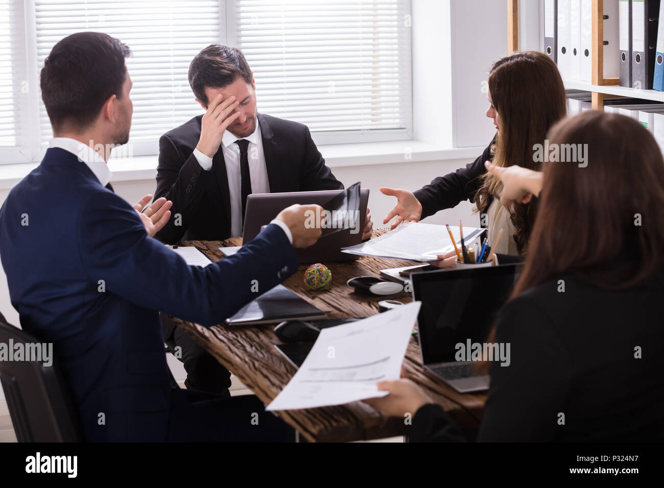 Businesspeople Blaming Depressed Young Male Colleague At Workplace ...