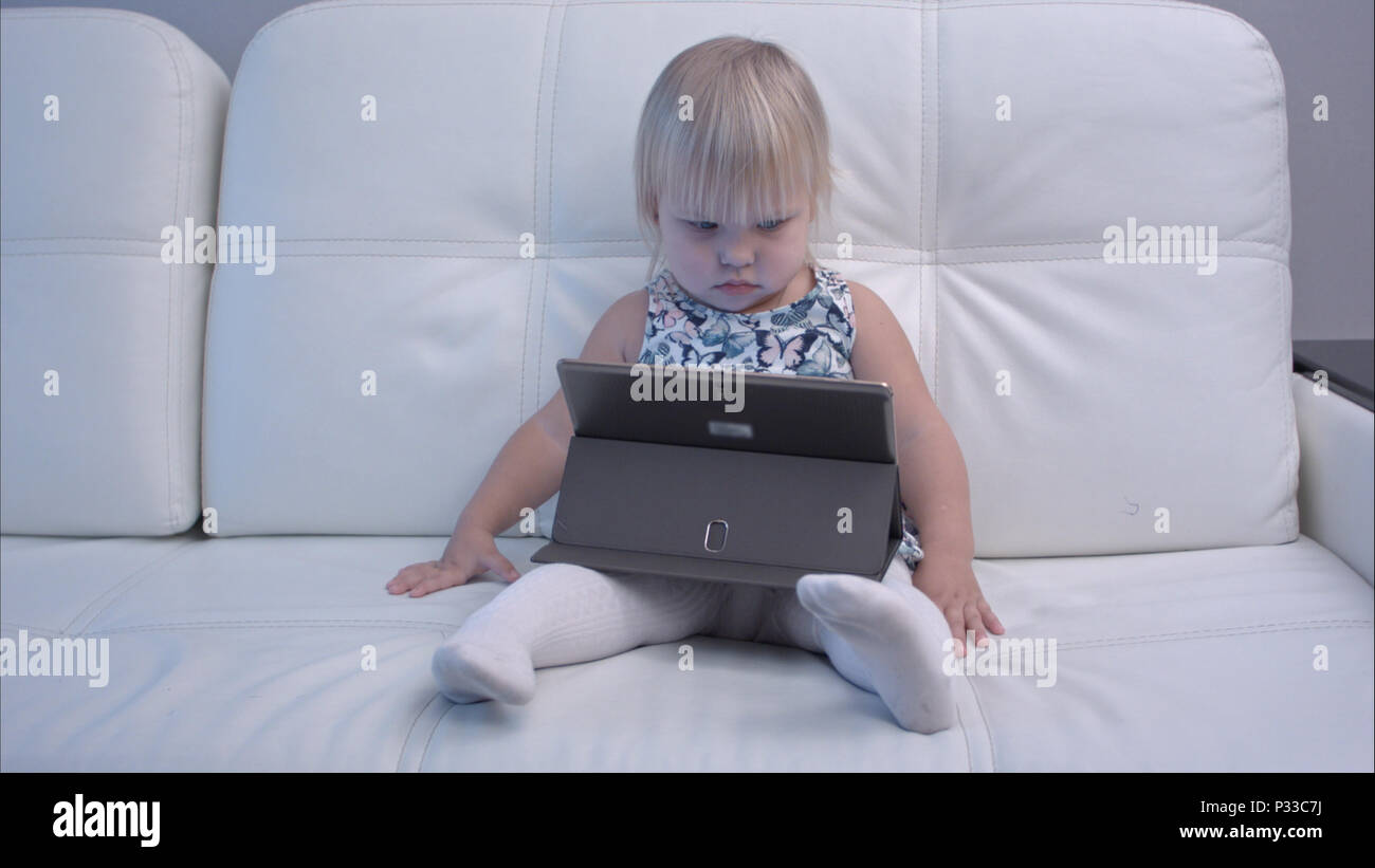 Serious baby girl playing with tablet Stock Photo - Alamy