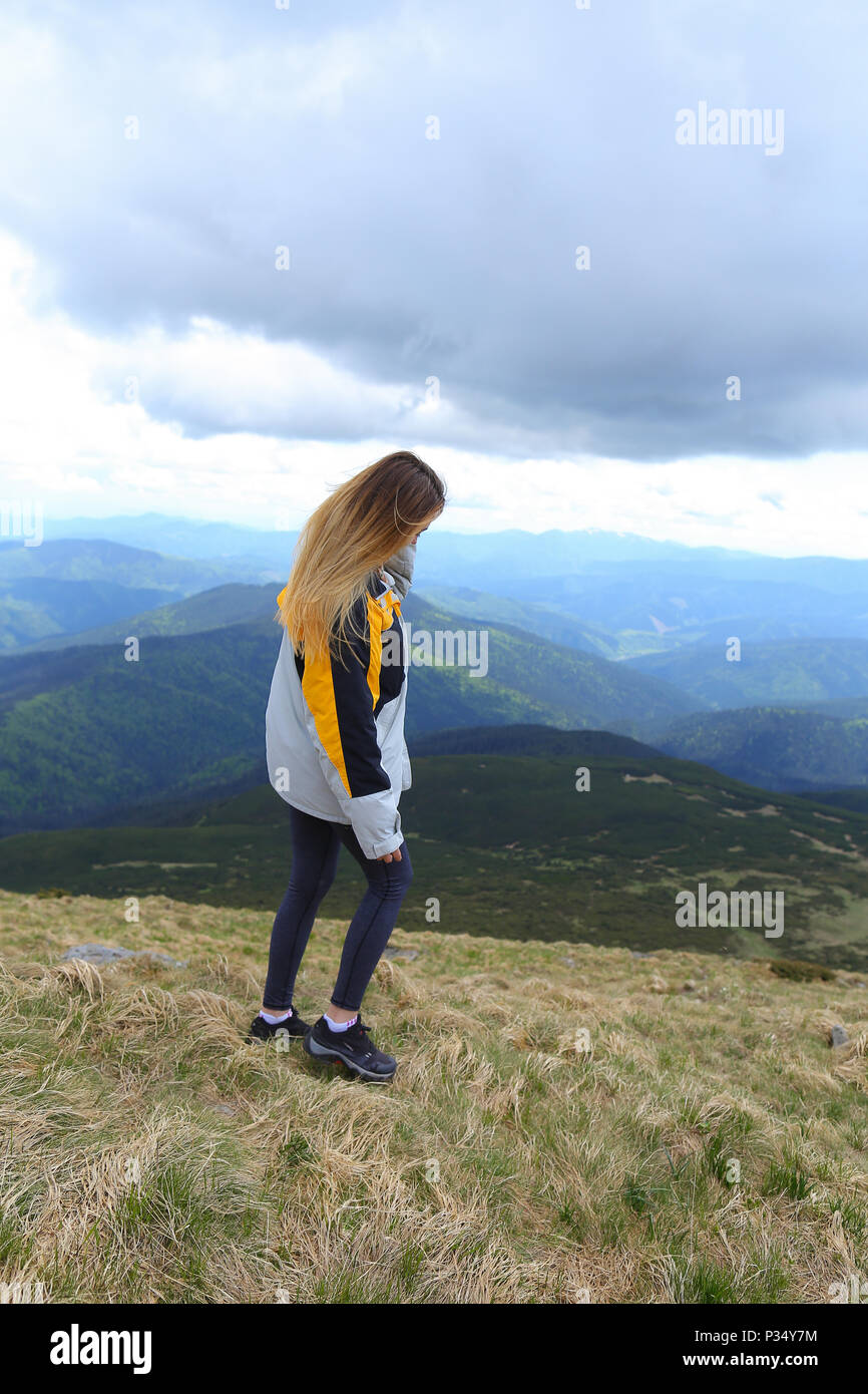 Blonde female tourist wearing yellow jacket standing in Alps mountains ...
