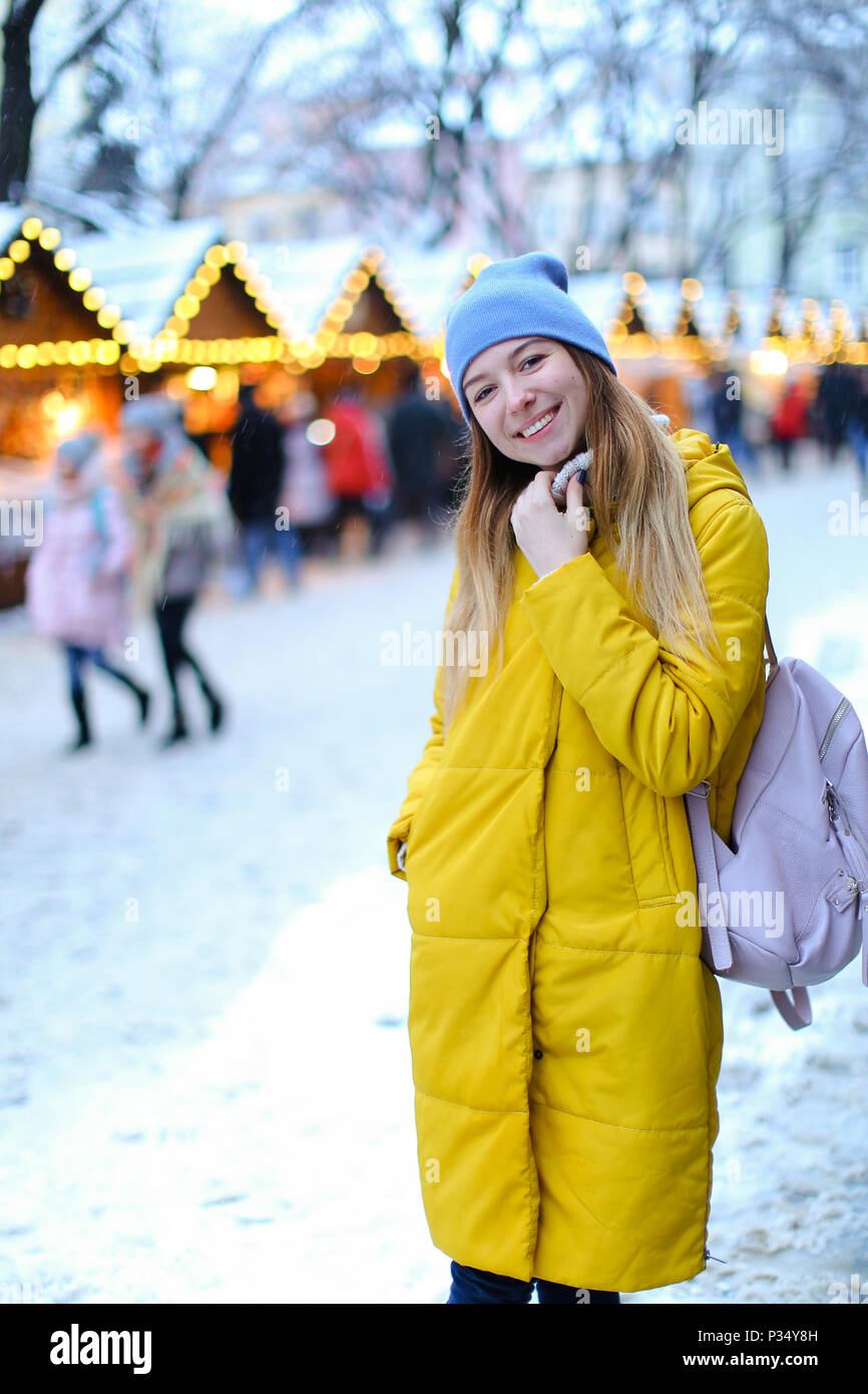 Young student wearing yellow coat, backpack and cap walking on snow ...