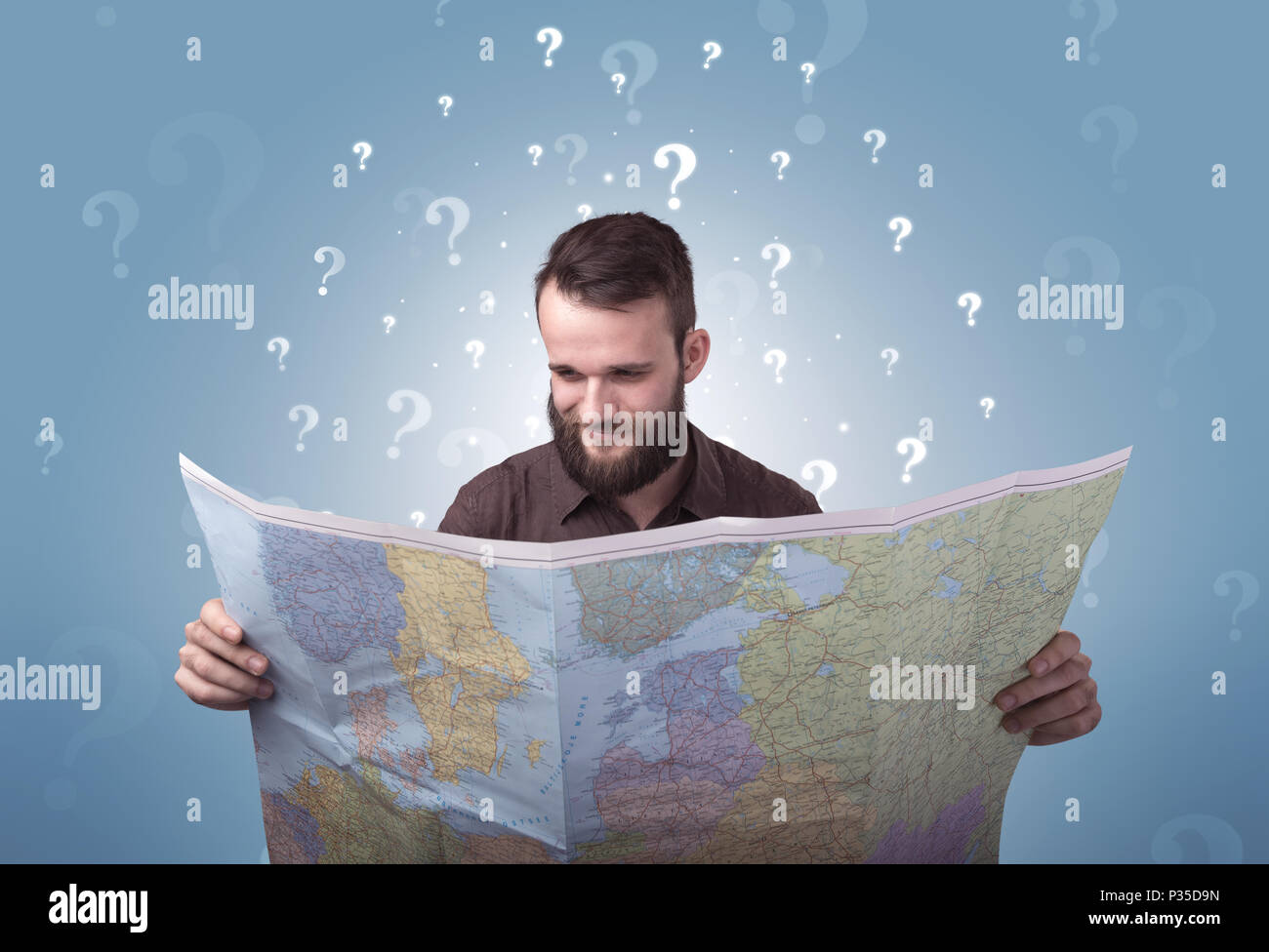 Handsome young man holding a map with white question marks above his ...
