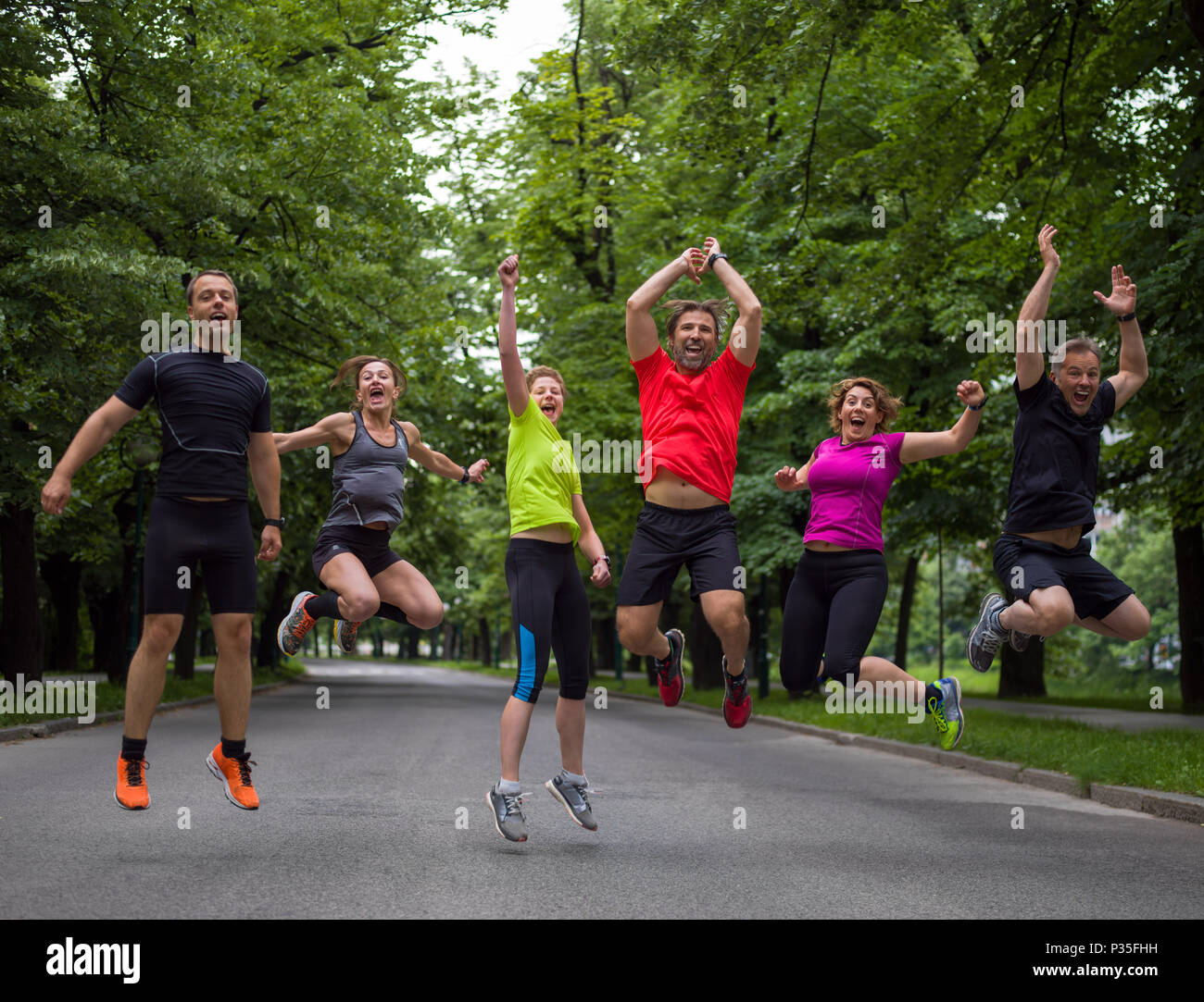 group of healthy runners team jumping in the air at city park during ...