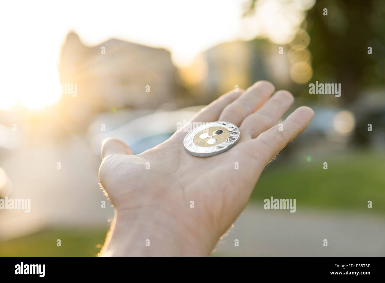 Golden silver Ripple coin in hand on a blurred sunset background. Hand ...