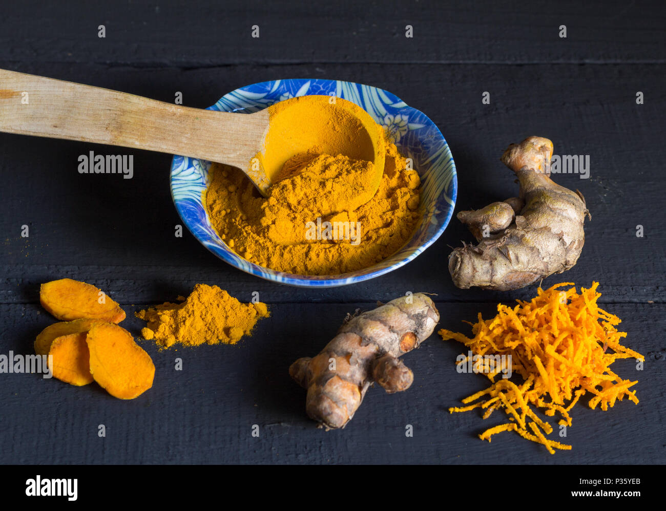 Turmeric root and grated fresh turmeric with powder and wooden scoop on ...