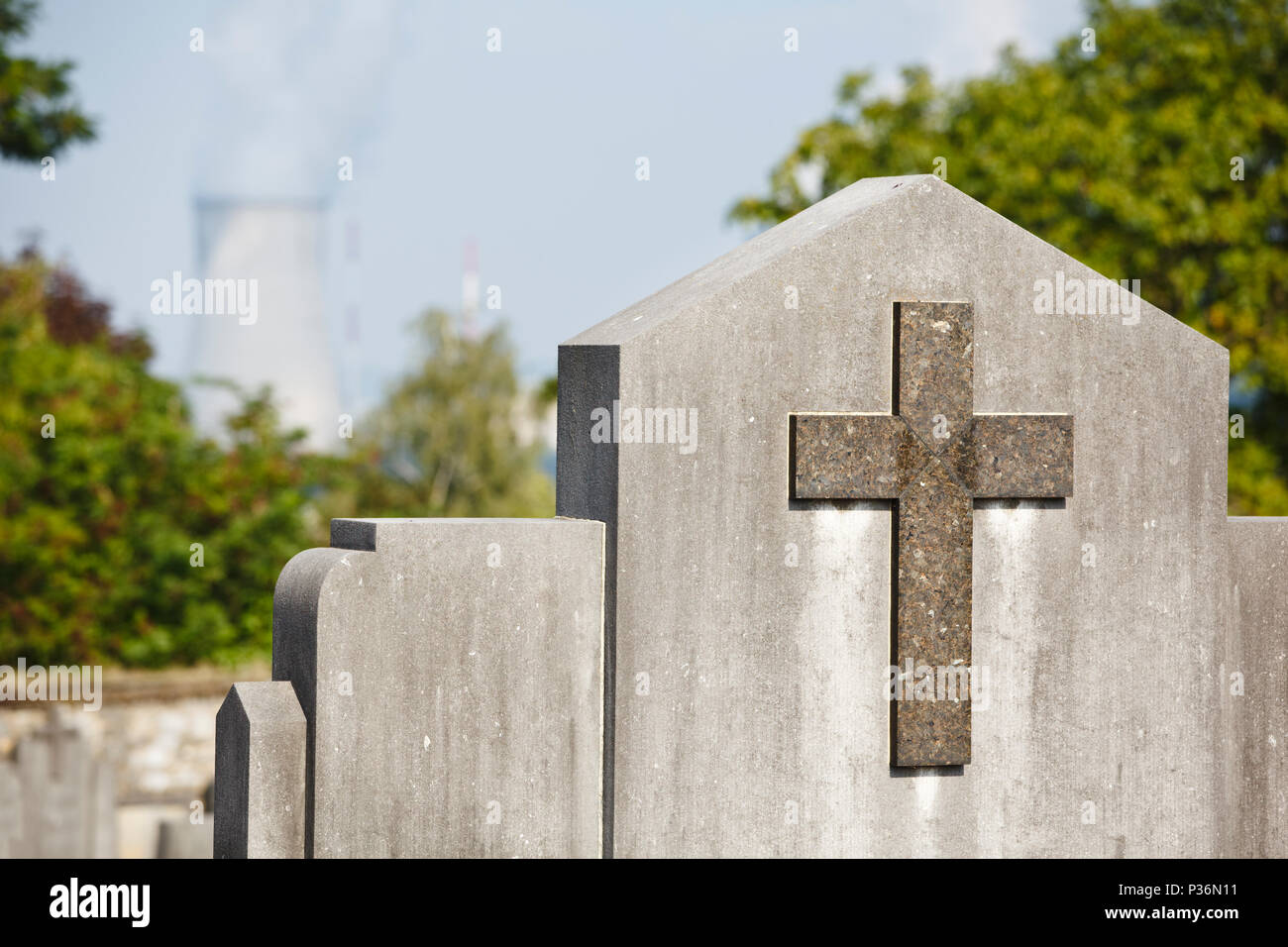 A tombstone with a cross on a cemetery, a nuclear power station in the ...