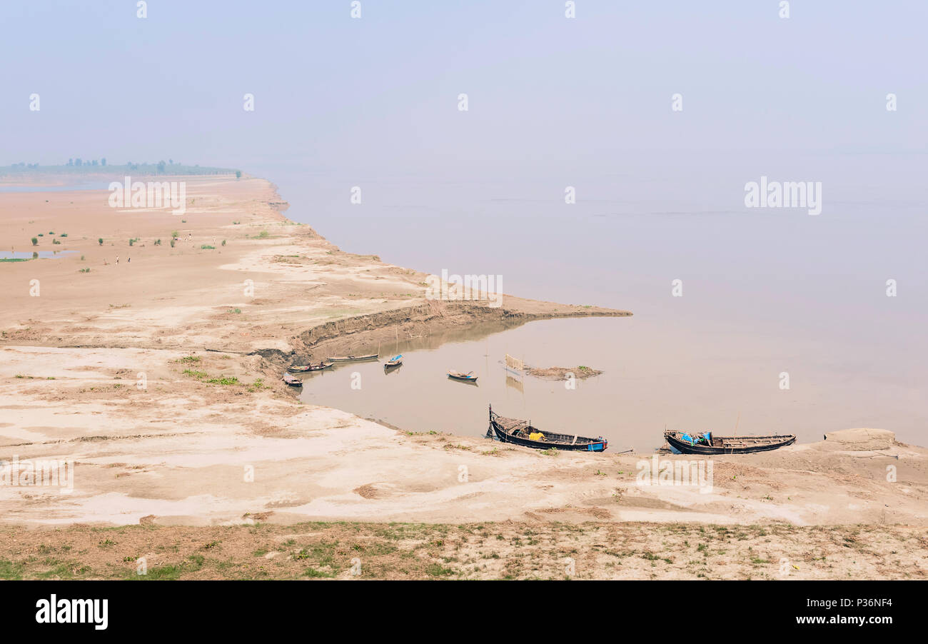 The river Ganges with boats moored along the bank and mud flats on a ...