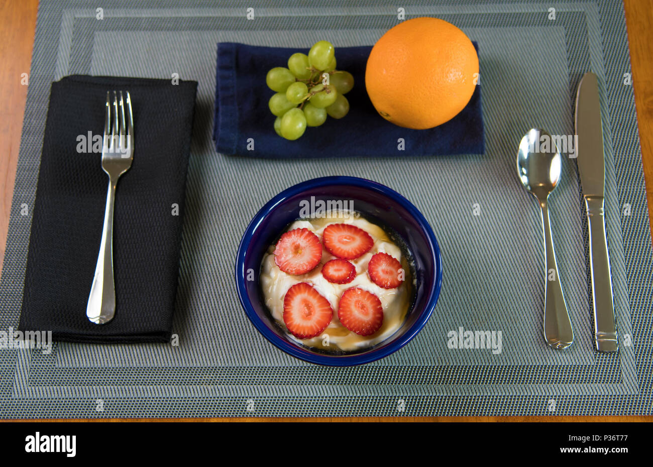 Horizontal food shot of grapes, an orange and yoguhrt with strawberries ...