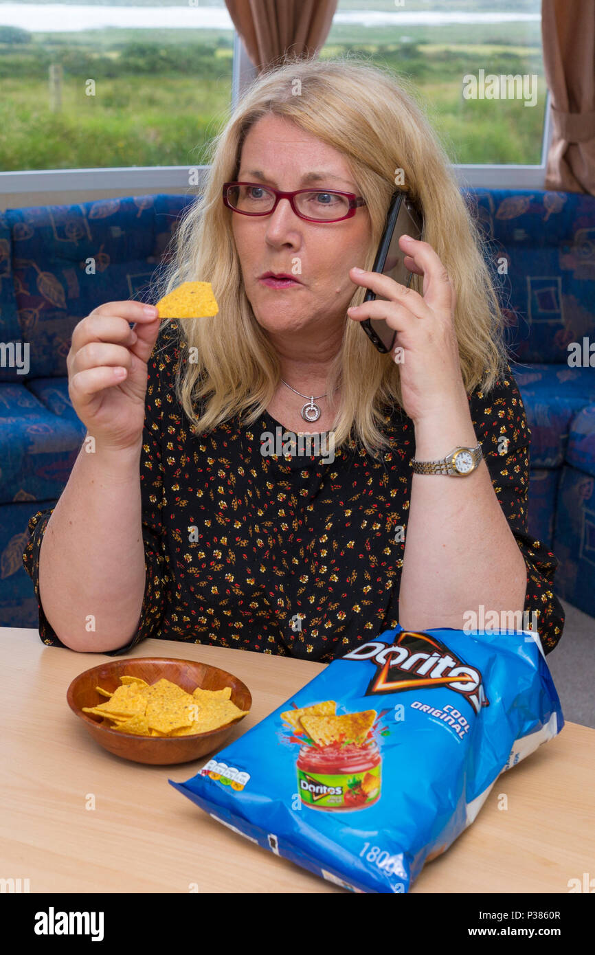 Blond woman eating Doritos from a sharing size bag and a small bowl ...