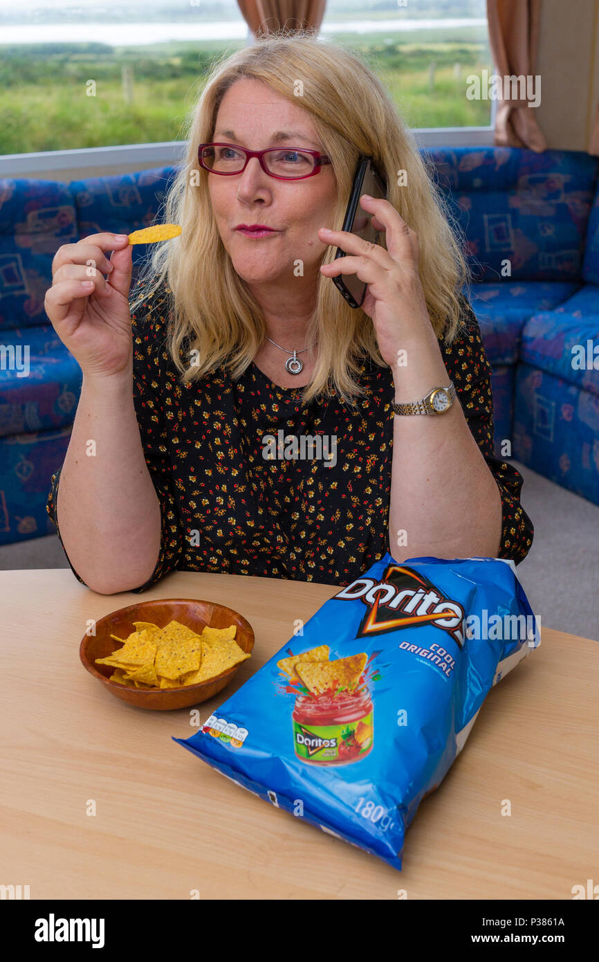 Blond woman eating Doritos from a sharing size bag and a small bowl ...