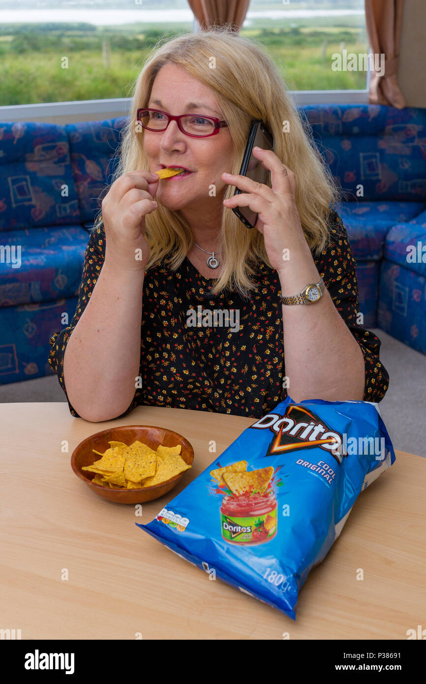 Blond woman eating Doritos from a sharing size bag and a small bowl ...