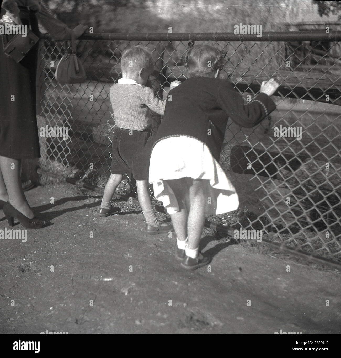 1950s, a small bo in shorts and sandals standing up and an older girl ...
